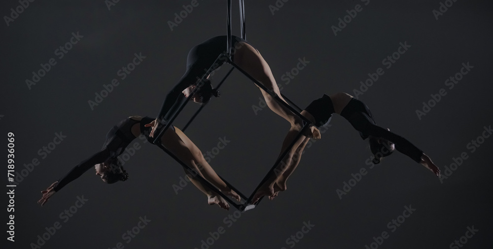 Trio of young female acrobats posing on a cube suspended at a height ...