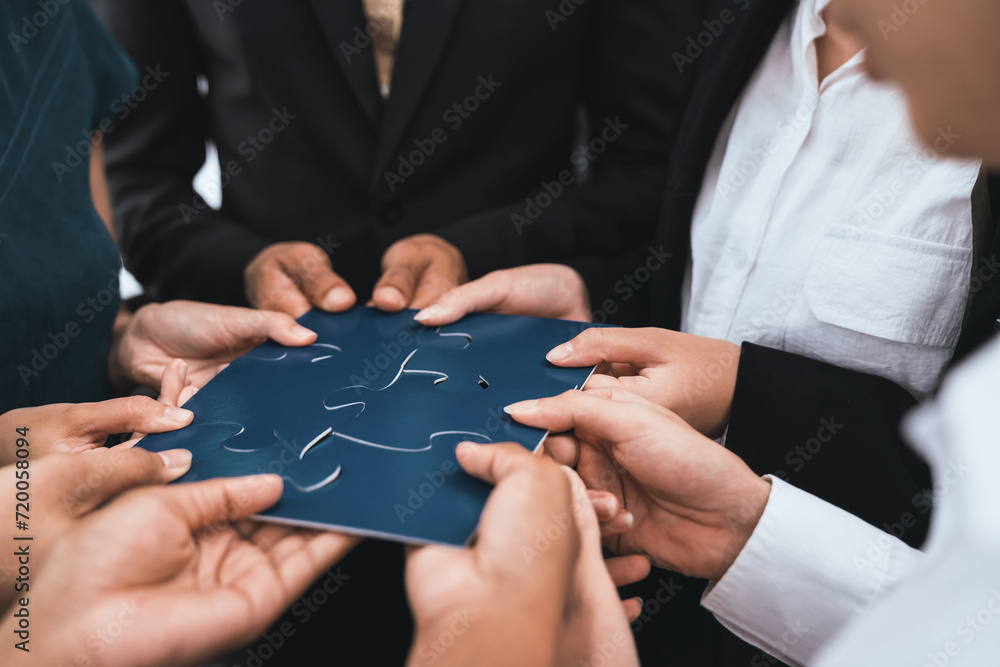 Diverse corporate officer workers collaborate in office, connecting puzzle pieces to represent ...