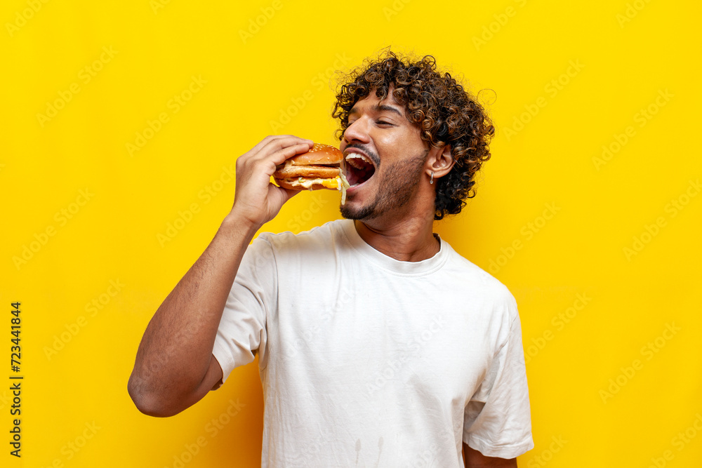 young indian man eating a big tasty burger with his mouth wide open on ...