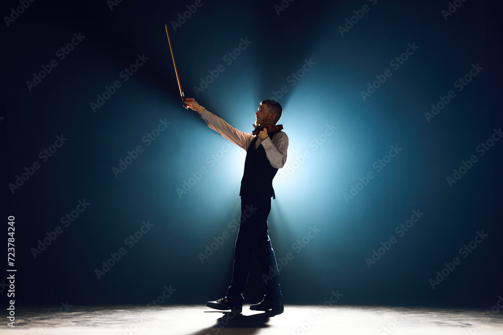 Solo violin performance, musician player in dark venue stands on stage ...