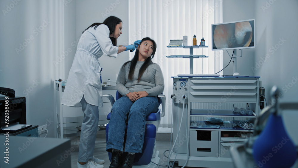 Female doctor otolaryngologist examines ear of Asian woman using ...