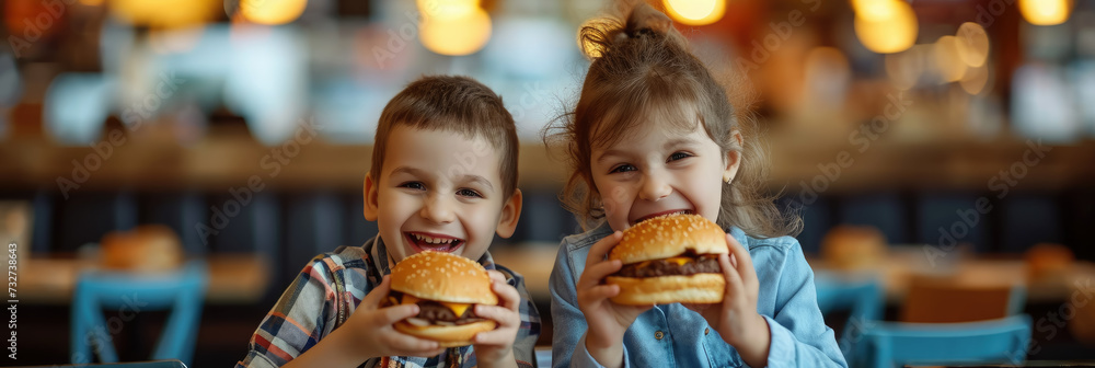two little children eating a big hamburger at a table in a cafe, boy ...