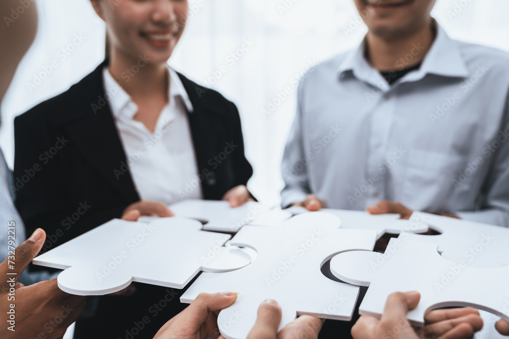 Diverse corporate officer workers collaborate in office, connecting puzzle pieces to represent ...