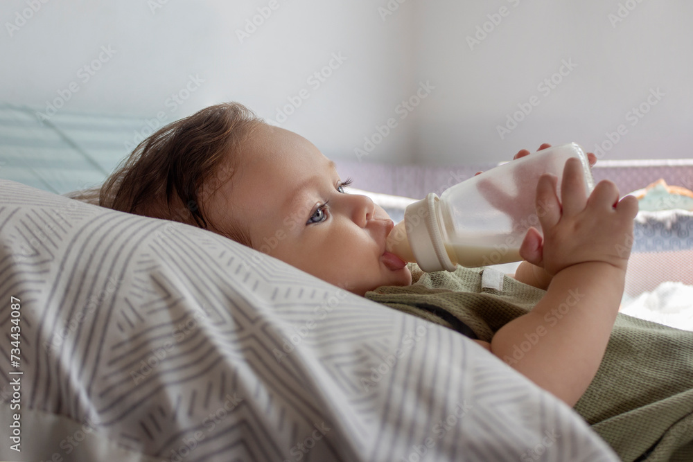 Bebé varón echado en su cama tomando su biberón con leche en su ...