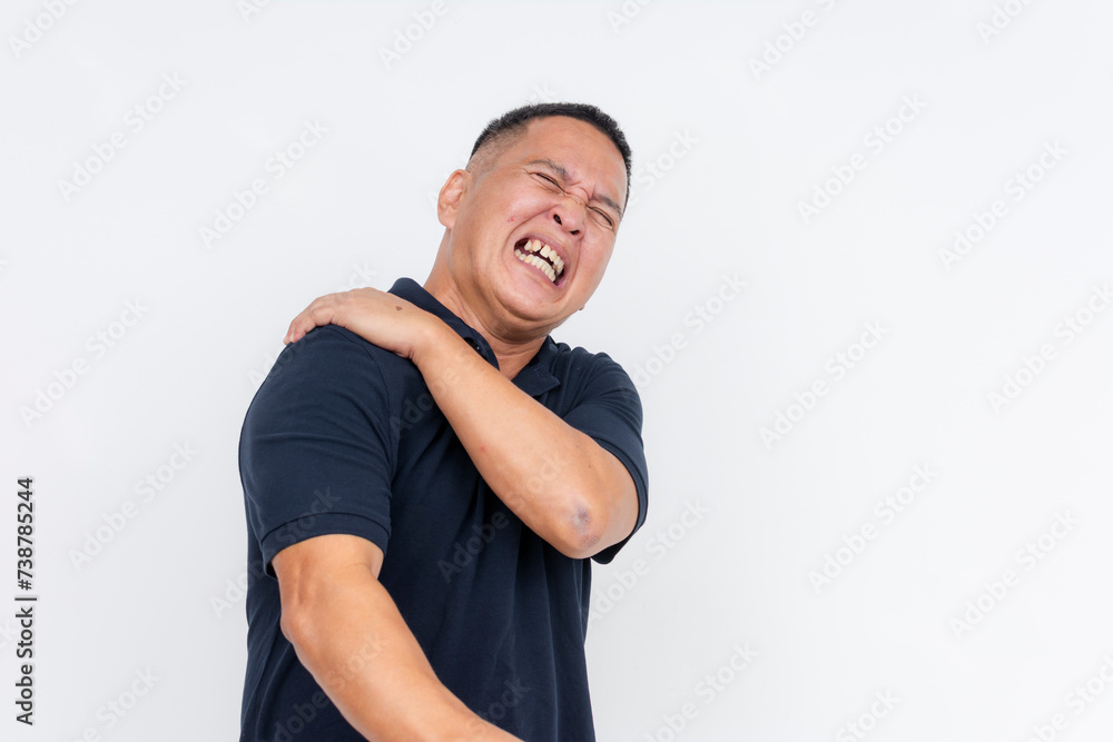 Asian man in pain, wincing as he holds his stiff shoulder, depicting ...
