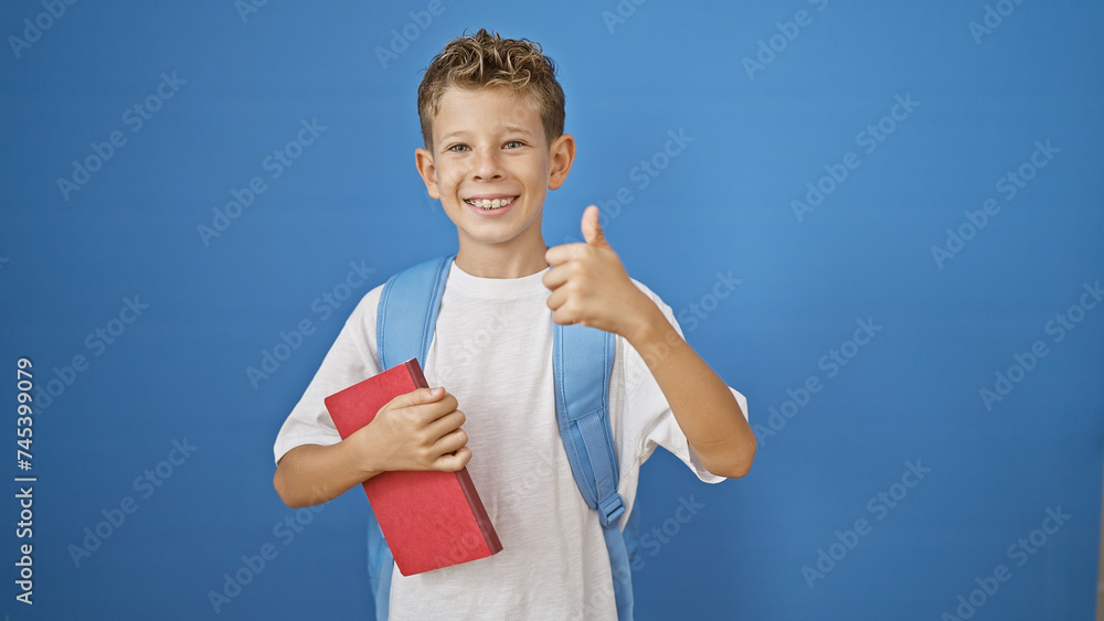 Adorable blond boy student, confidently holding book while giving thumb ...