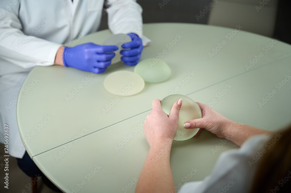 Close-up of female plastic surgeon demonstrates breast implants to a ...
