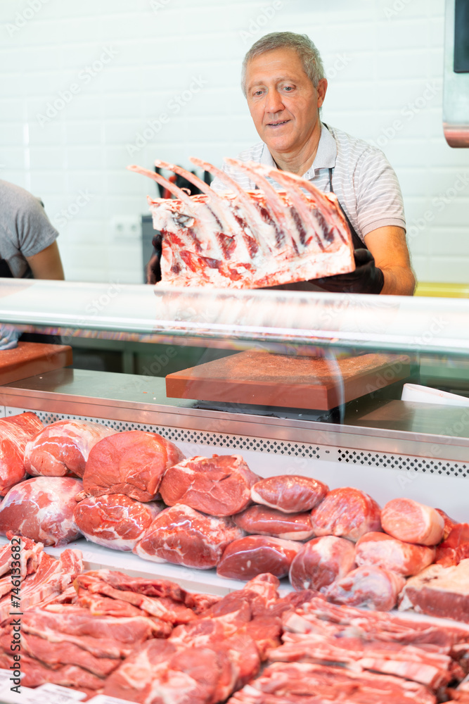 Smiling experienced aged butcher working behind counter in butchery ...