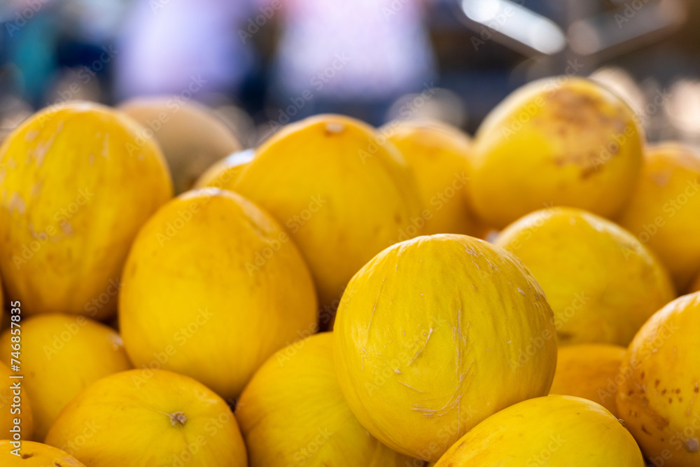 A bin of elongated vibrant yellow canary melons. The rind or skin is ...