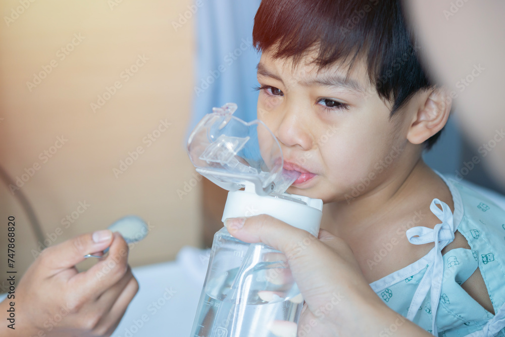 Shot view of little sick Asian boy is crying while drink water from a ...