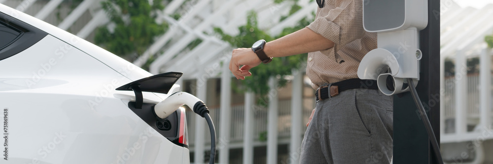 Young man checking time on smartwatch while EV charger to recharging ...