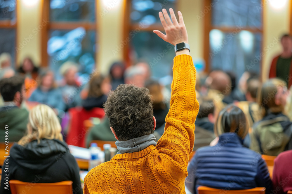 person with hand up to talk at local town hall meeting, from back view ...