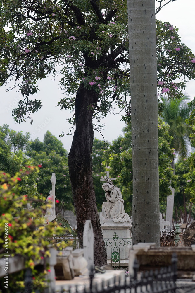 Marble statue of a nice young woman kneeling while hugging a cross atop an imposing grave in the ...