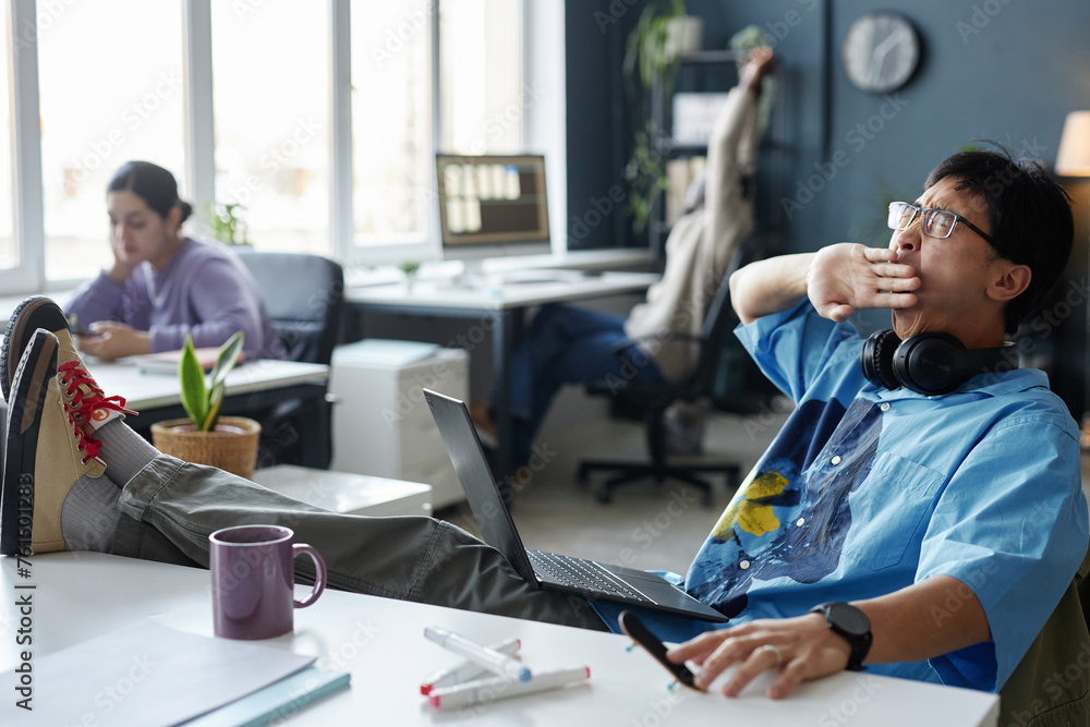 Side view portrait of Asian young man yawning while working with laptop ...