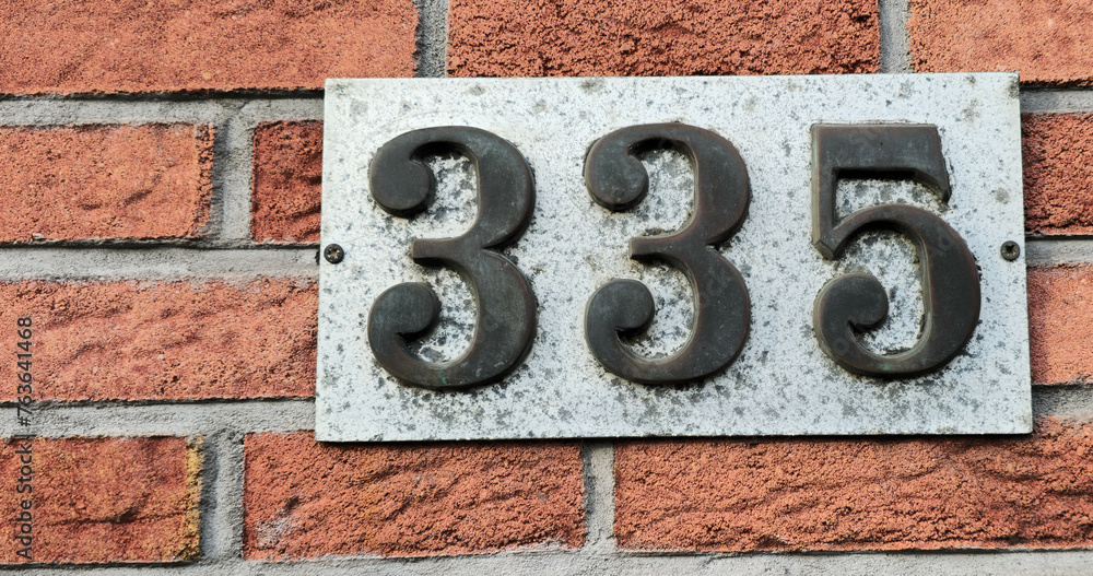 Number plate. Number 335 against a red brick wall background. Concept ...