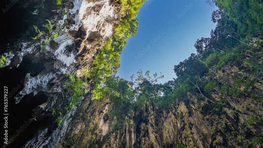 The clear blue sky is visible in a frame formed by sheer cliffs. Green ...