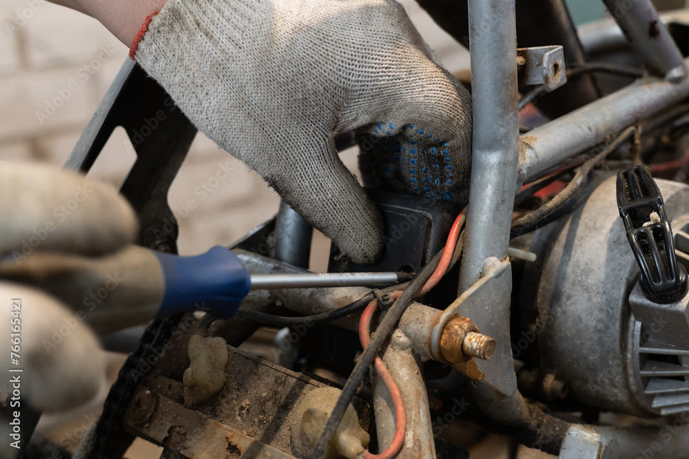 In the garage, a man is repairing a children's ATV and replacing broken ...