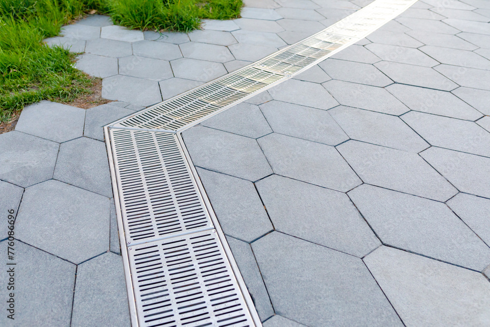 Metal storm sewer grate on shaped paving slabs in park. Drainage ...