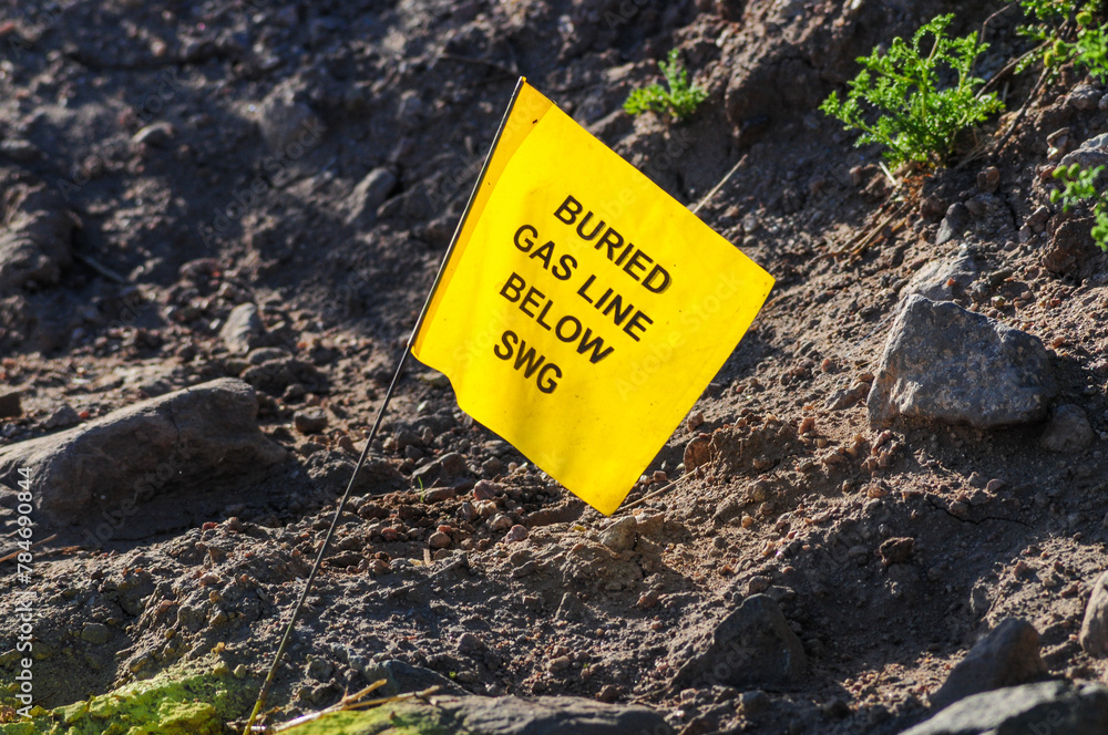 Bright yellow "Buried Gas Line Below" warning flag stand on a dirt lot ...