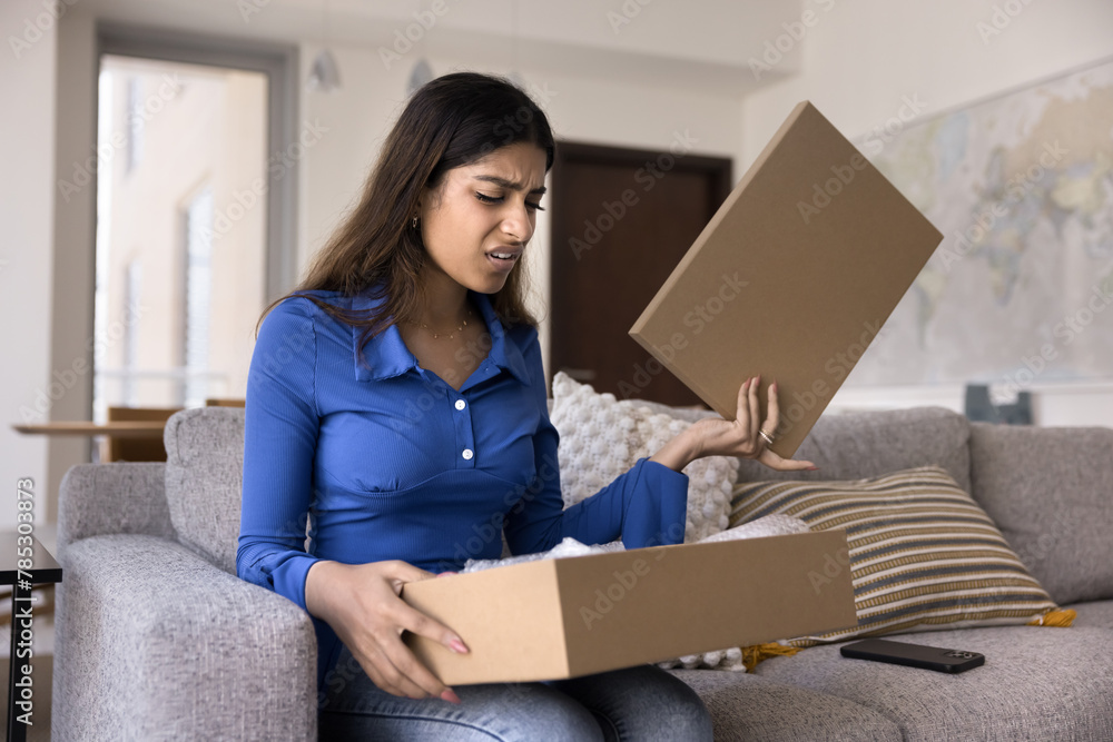 Upset concerned young Indian customer woman opening logistic cardboard ...