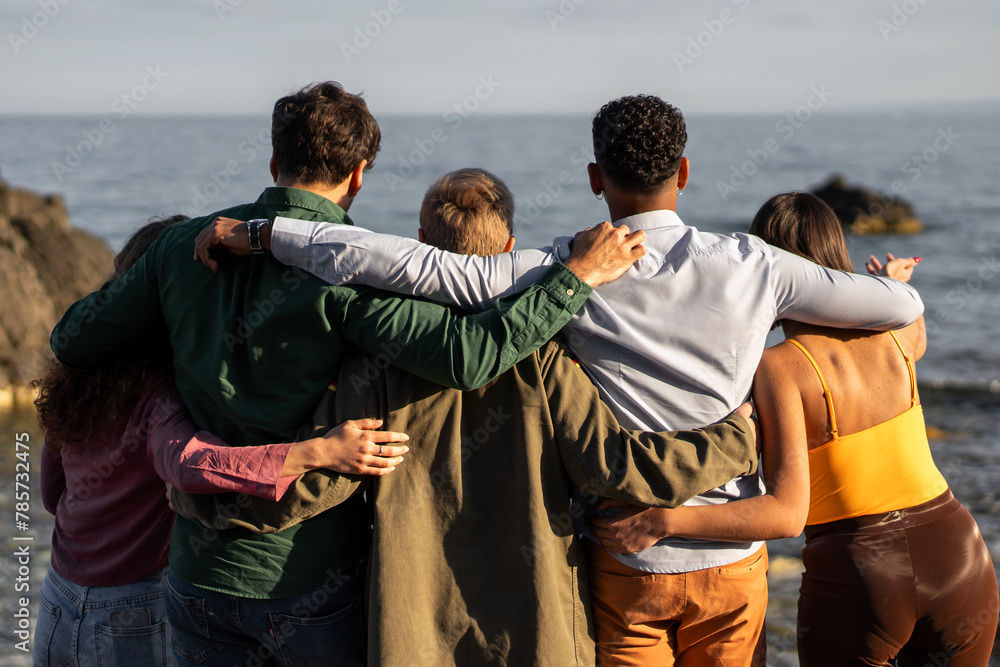 A tight-knit group of friends stands together, gazing out at the sea ...