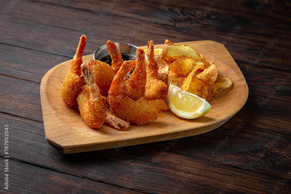 Battered king prawns with barbecue sauce and potato chips on dark ...