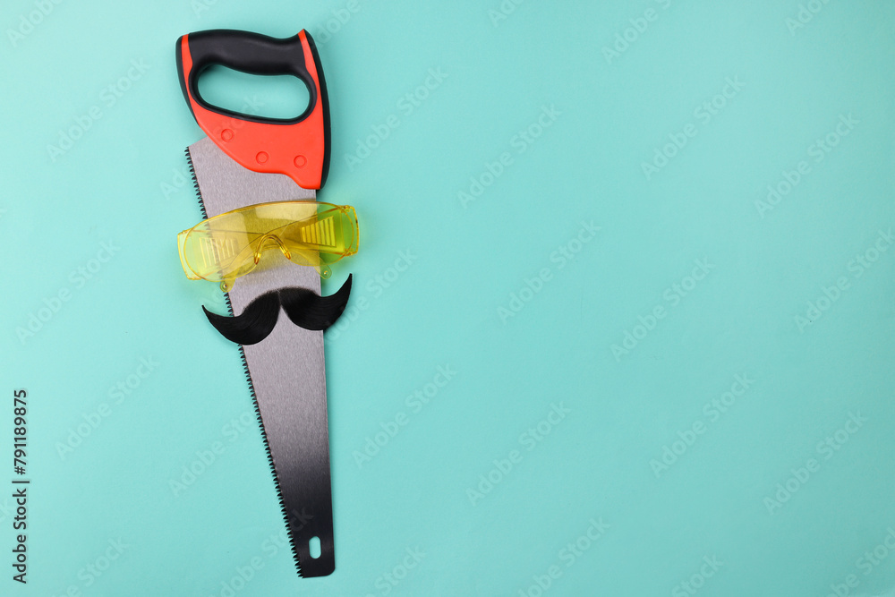 Man's face made of artificial mustache, safety glasses and hand saw on ...