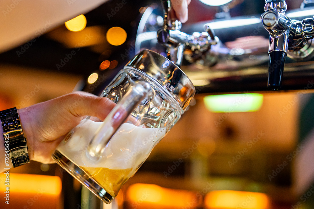 Dynamic scene in a pub with a bartender pouring frothy beer from a tap into a clear mug ...