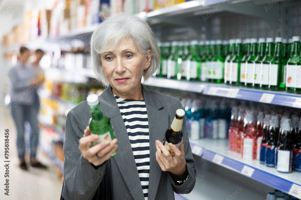 Positive senior lady choosing alcoholic beverage at local liquor store ...