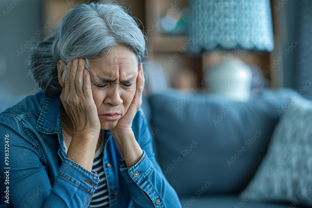 An anguished elderly woman with gray hair, sitting on the sofa at home ...