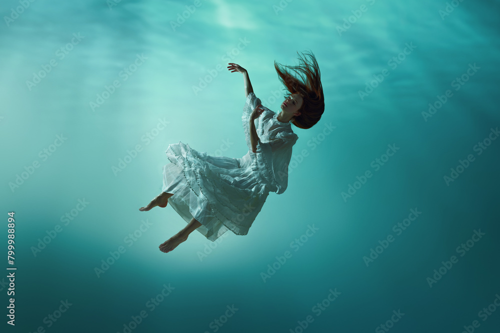 Fairy-like image showing underwater mysterious scene with elegant young ...