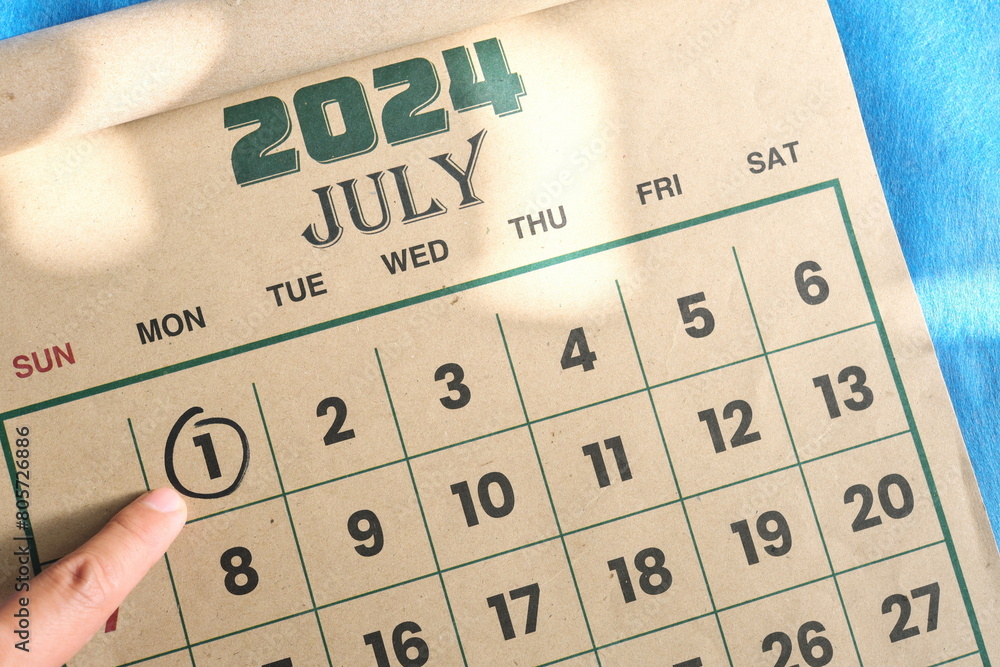 Hand pointing on July 1 2024 date on calendar flat lay in blue ...