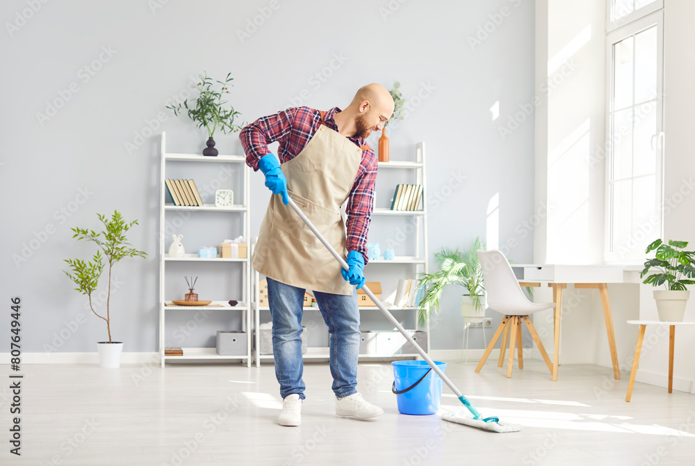 Happy man wearing in apron and gloves is cleaning the home and mopping ...