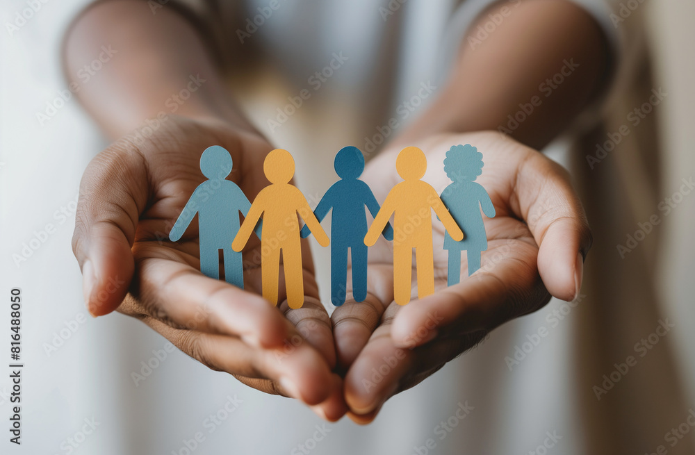 Hands gently holding colorful paper cutouts of diverse family figures, symbolizing unity ...