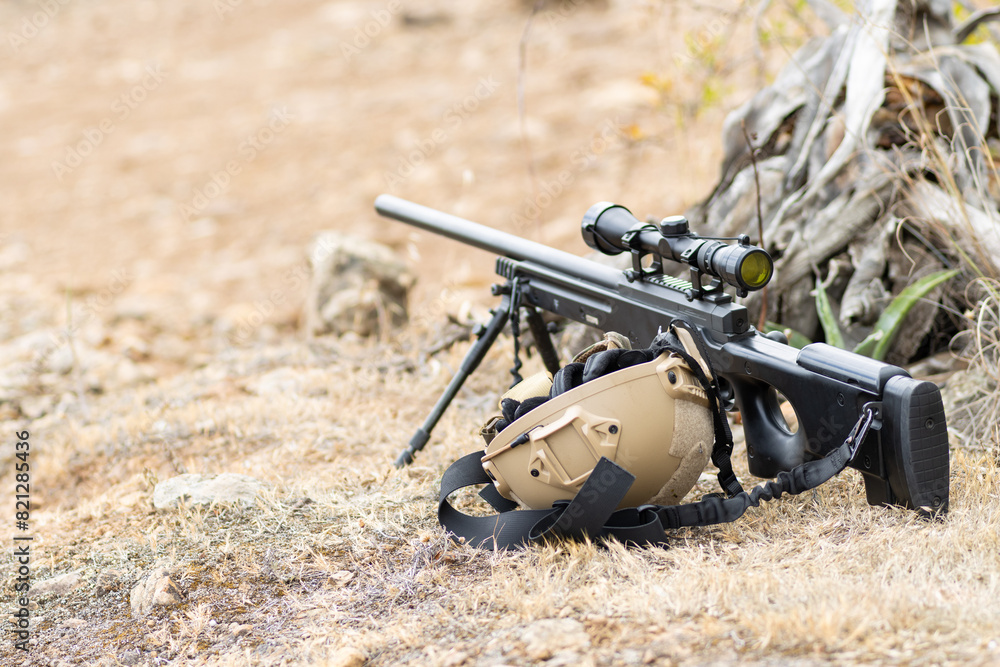 Black sniper rifle with telescopic sight and airsoft helmet resting on ...