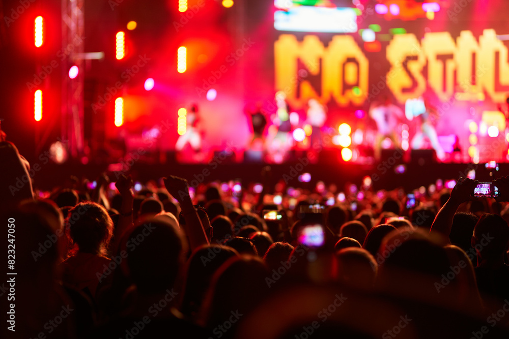 Energetic audience at night music fest, brightly lit stage ahead ...