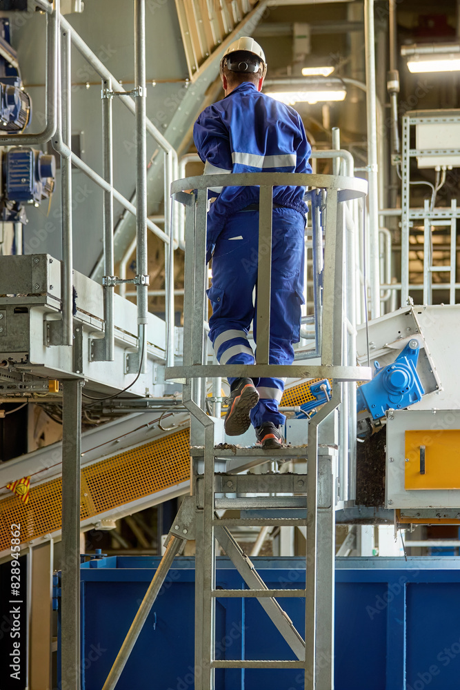 Worker in blue uniform and hard hat standing on a platform in an ...