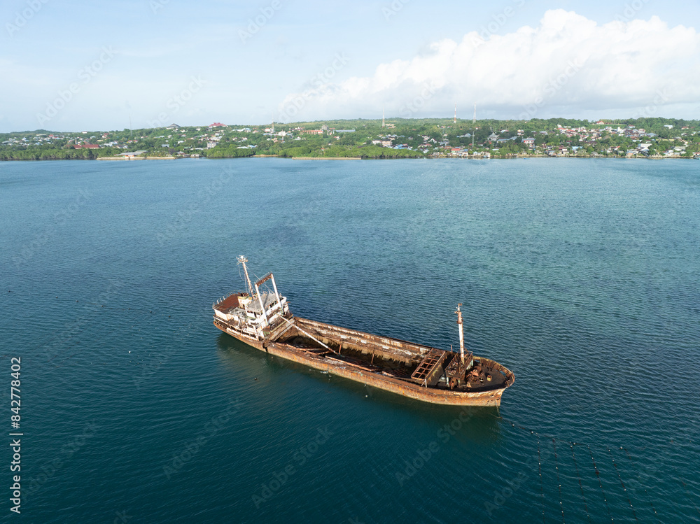 An old, rusted shipwreck has floundered in shallow water in the harbor ...