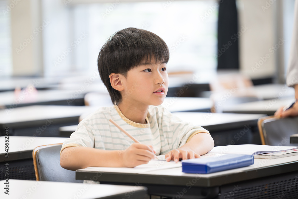 Elementary school boy studying and holding pencil during class in ...