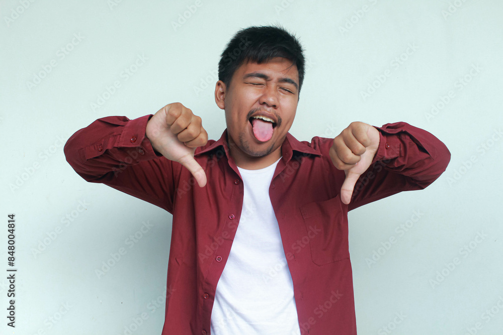 Scoffed Asian man wearing red shirt gives thumbs down hand gesture of ...