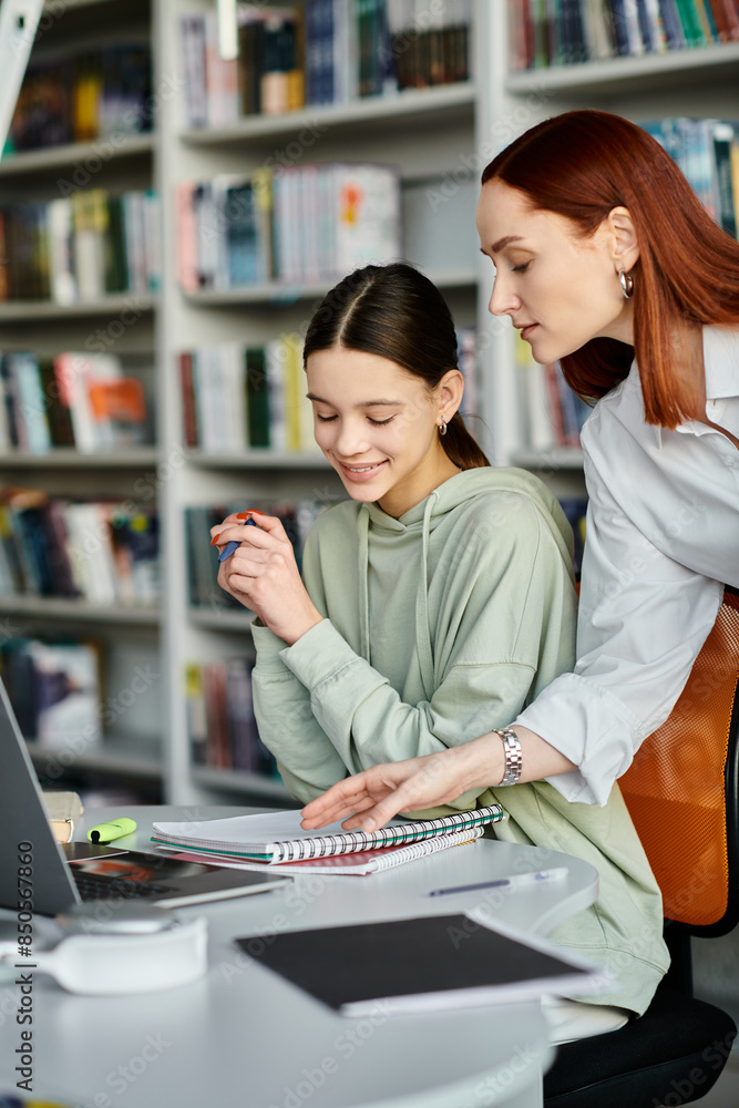 A tutor with red hair teaches a teenage girl in a library, as they work ...