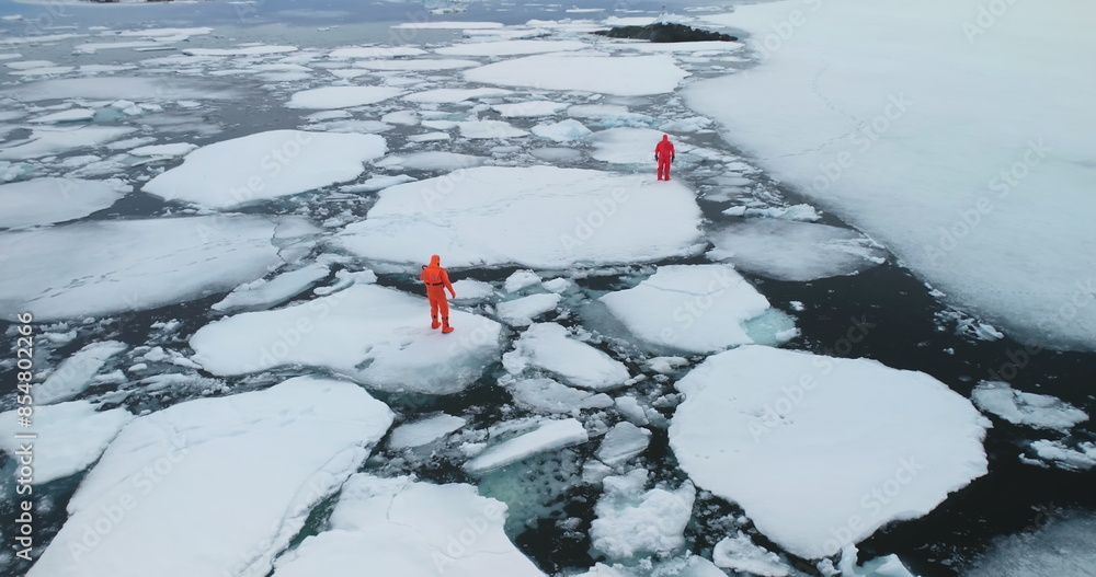 People in immersion suits on melted arctic ice. Two man in orange ...
