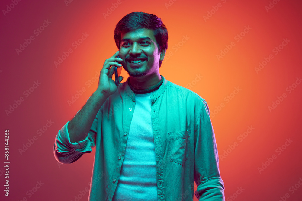 Smiling young Indian man looking at distance and talking on phone in ...