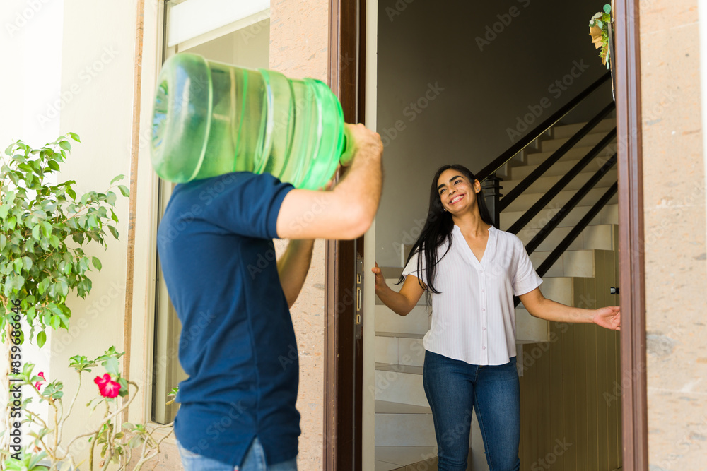 Delivery man carrying a heavy water jug and a smiling woman greeting ...