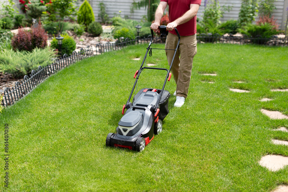 Man trimming overgrown green lawn with electric mower in garden ...