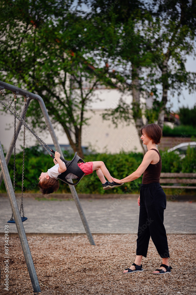 A mother pushing her son on a swing at the playground, both smiling and ...