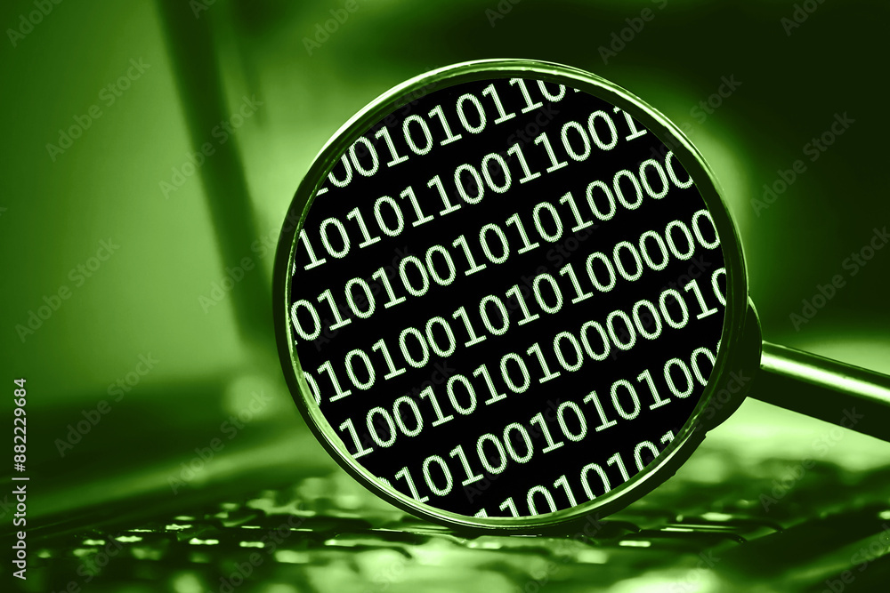 Magnifying glass over a laptop keyboard revealing binary code, creating ...