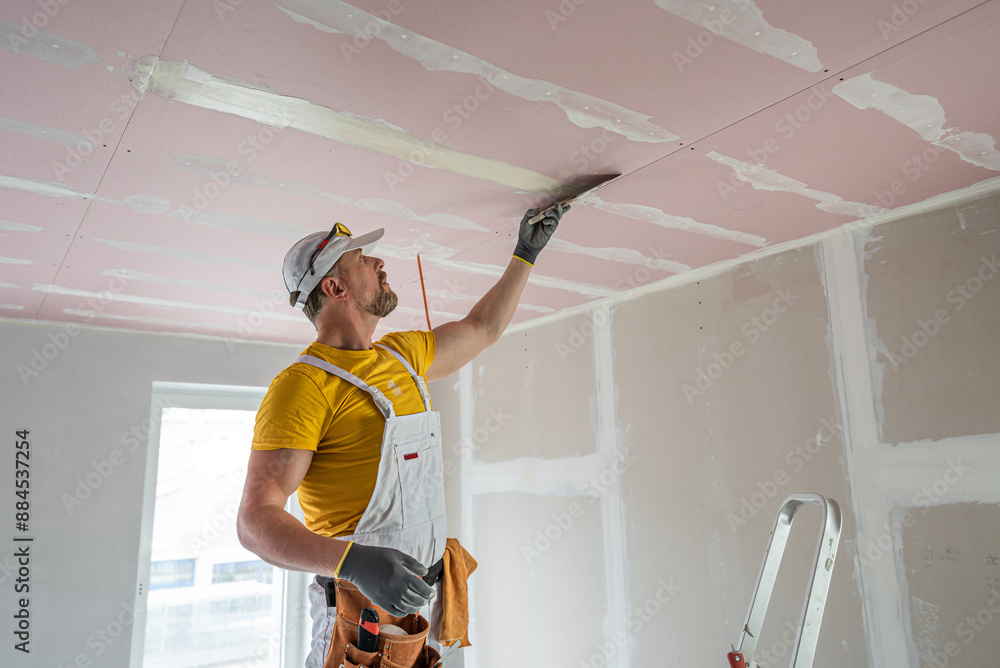 The worker make a plasterboard ceiling. He does taping plaster drywall ...