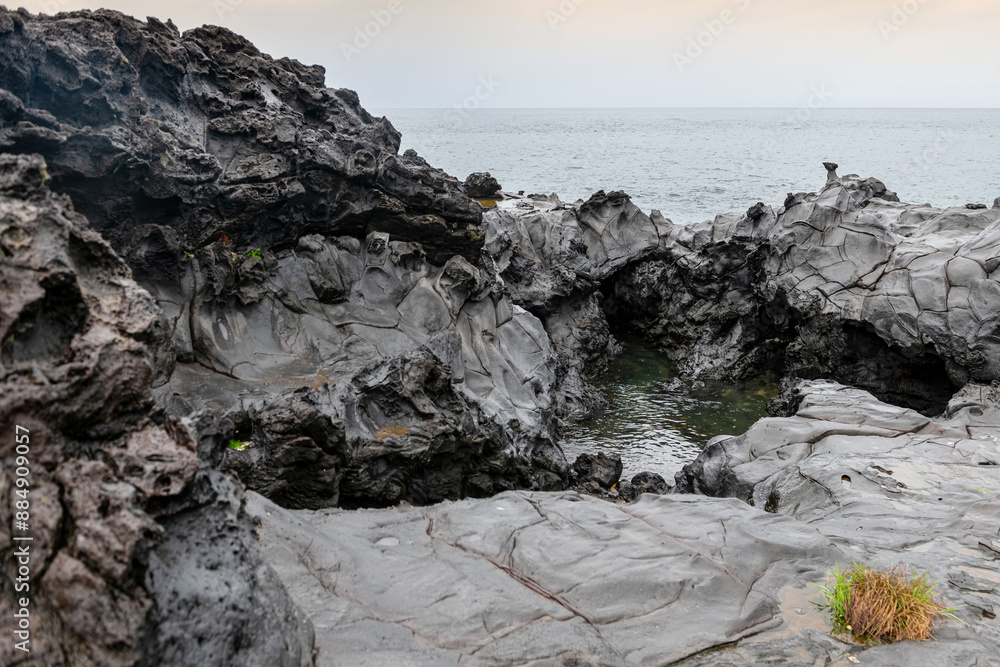 Summer view of water pool and wet volcanic rocks against sea near Gueom ...