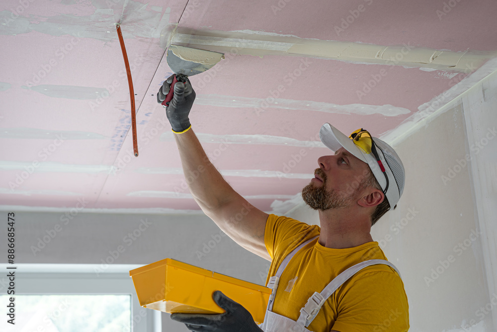 The worker make a plasterboard ceiling. He does taping plaster drywall ...